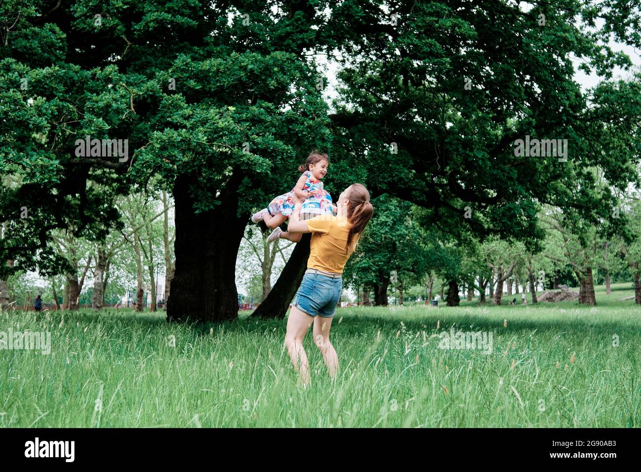 Mother lifting daughter while standing on grass in park Stock Photo - Alamy