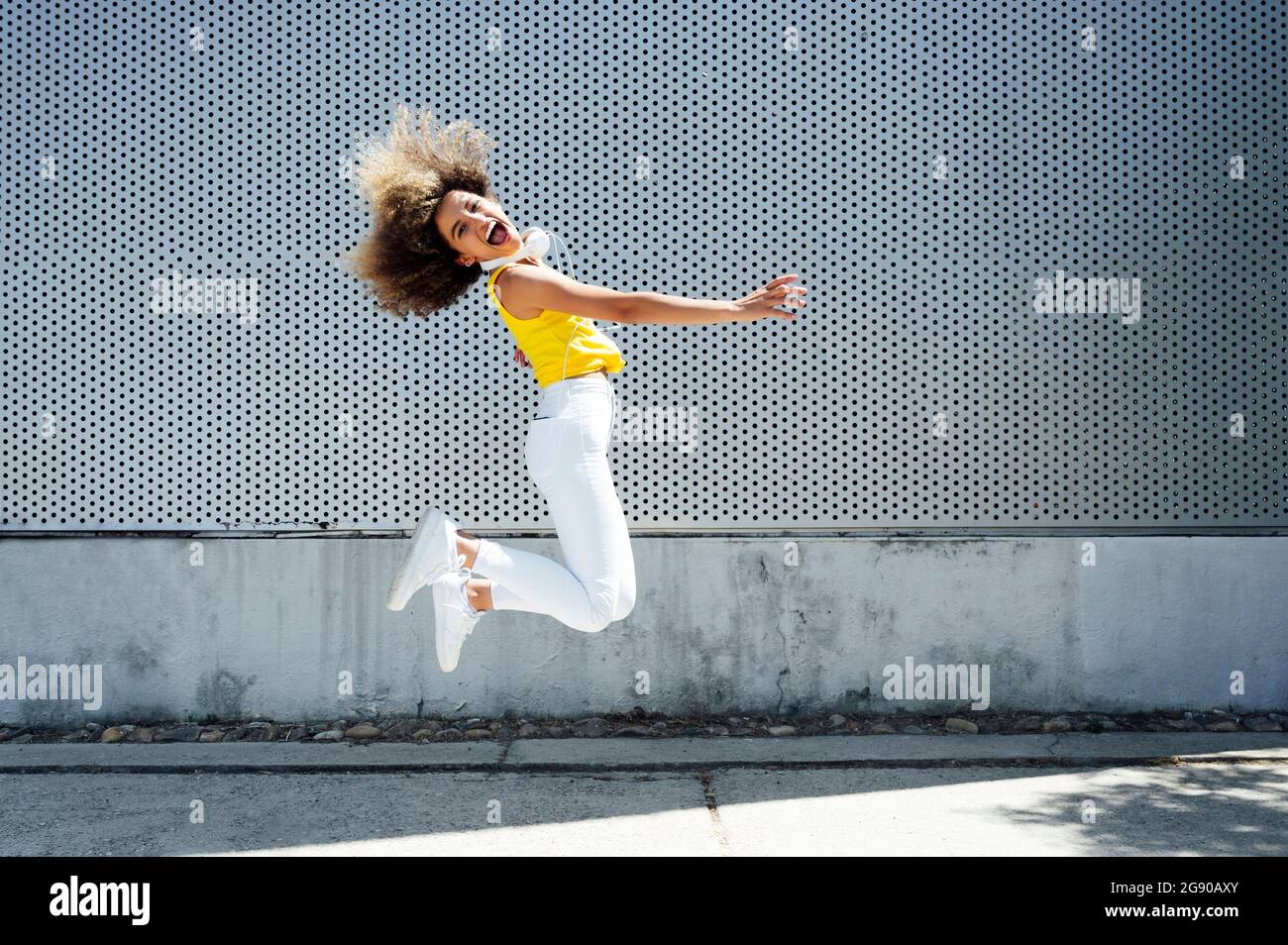 Happy young woman laughing while jumping on footpath Stock Photo - Alamy