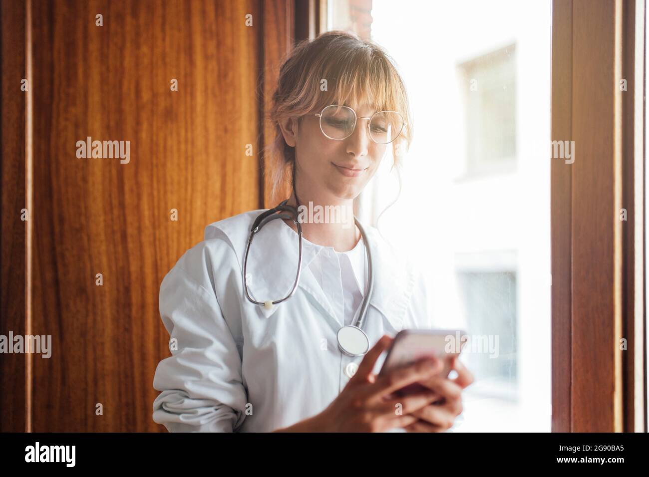 Female doctor using mobile phone by window in clinic Stock Photo - Alamy