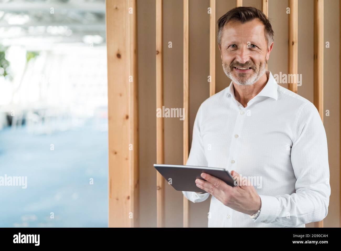 Businessman holding digital tablet while standing in front of wall ...