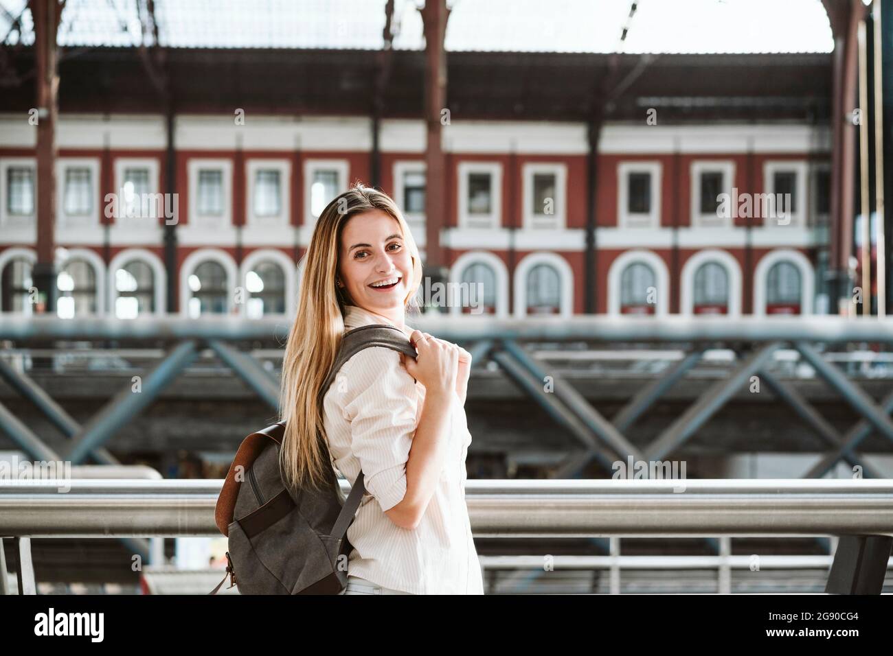 Happy blond woman wearing backpack st railroad station Stock Photo - Alamy