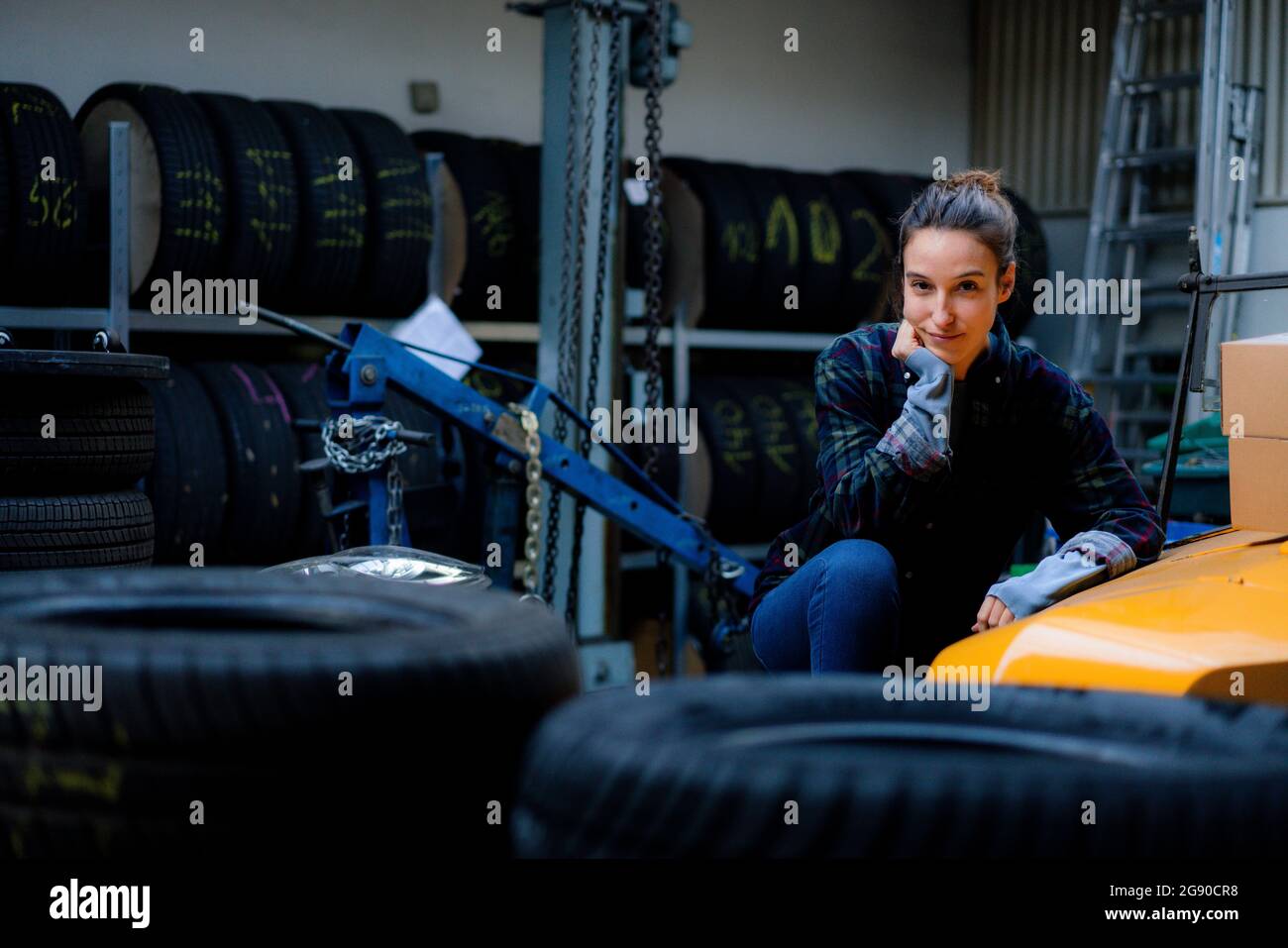 Female mechanic with hand on chin crouching by toy car at workshop ...