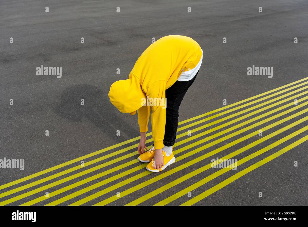 Boy touching toes while bending over yellow markings on road Stock ...