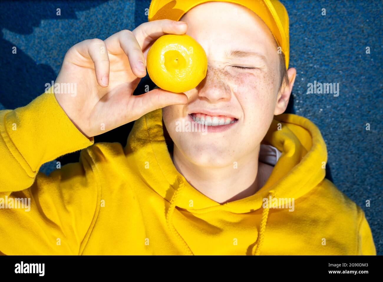 Smiling boy covering eye with lemon Stock Photo - Alamy