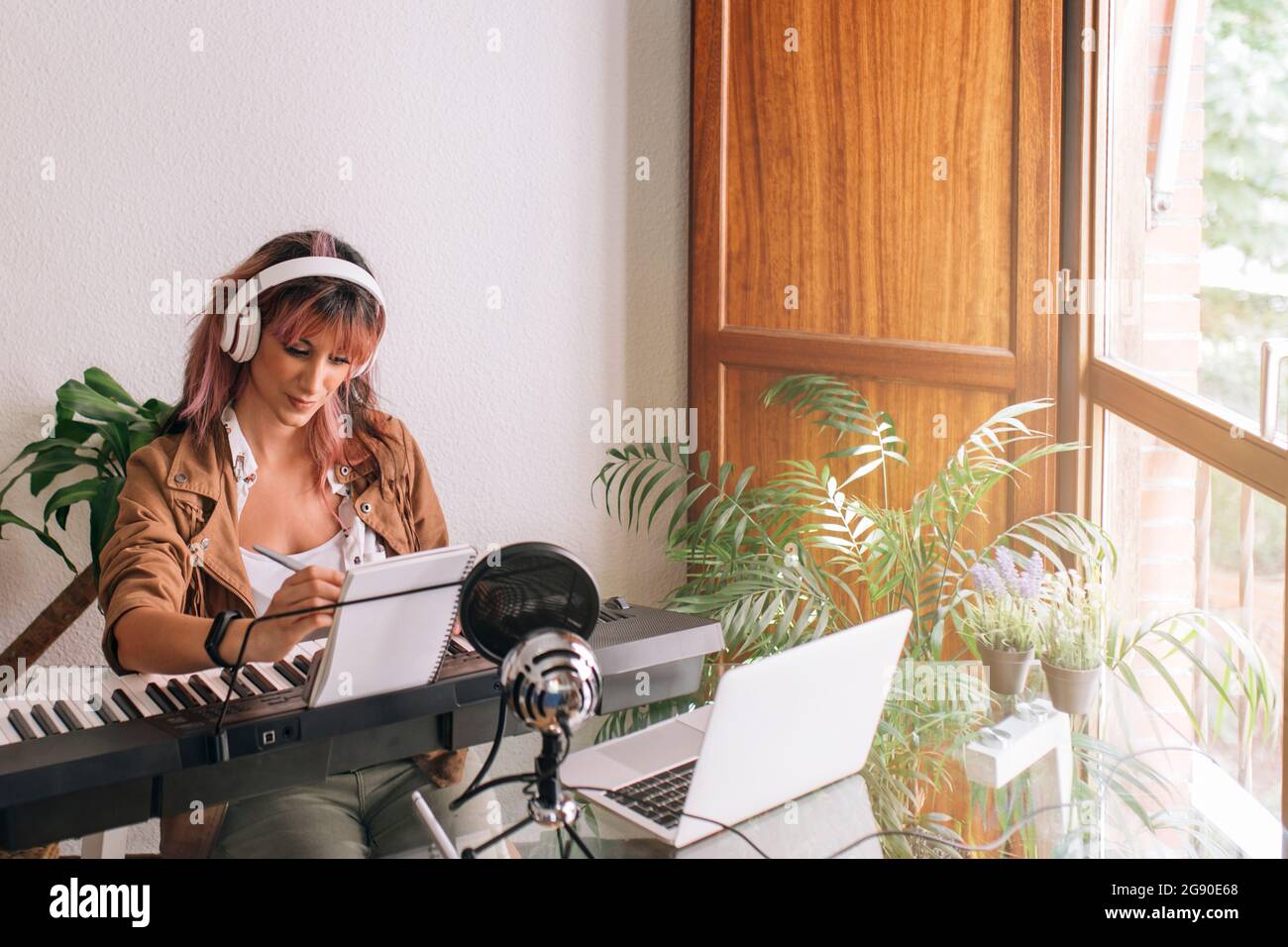 Female composer writing music notes in diary while practicing piano at ...