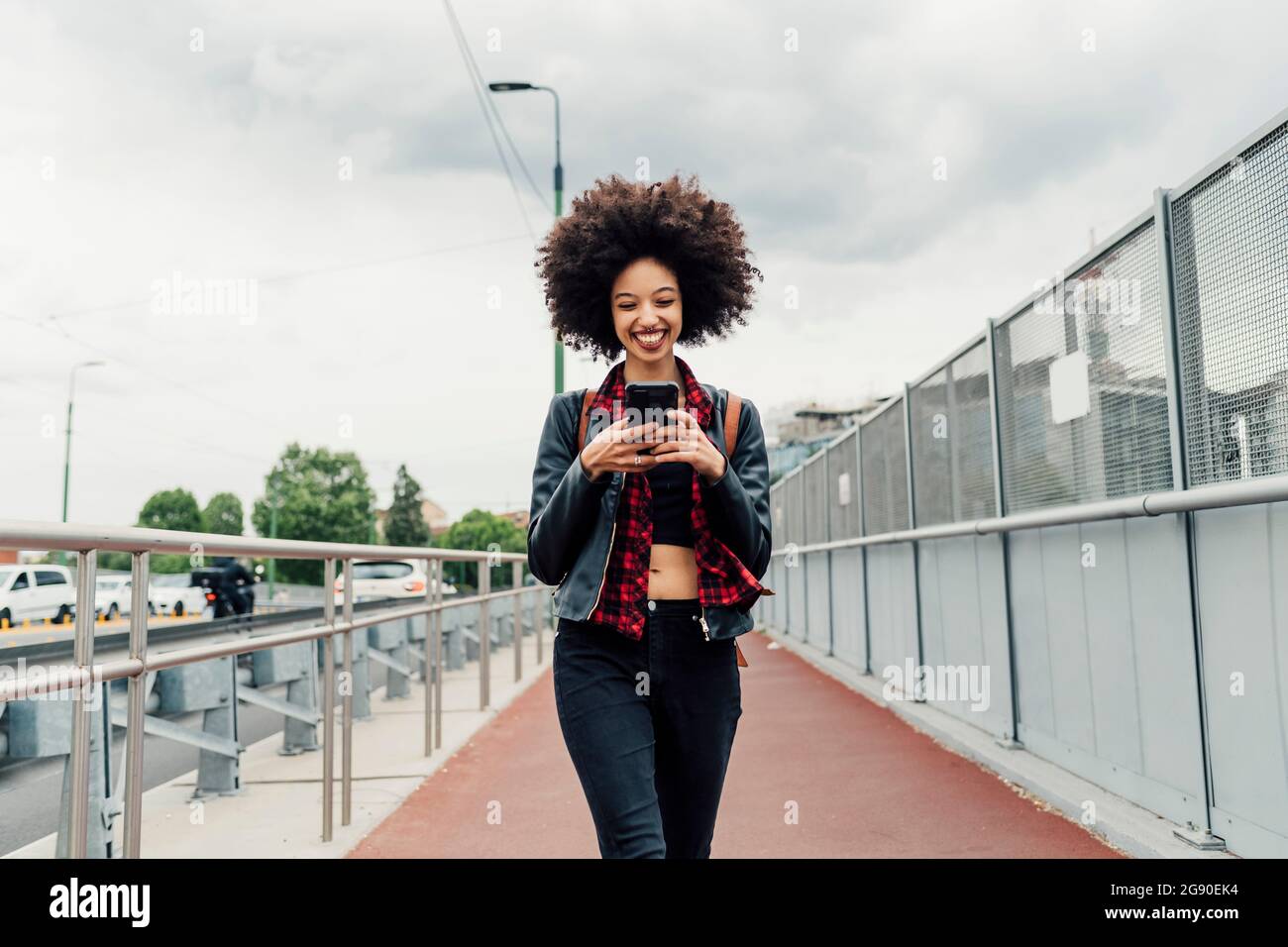 Happy woman using mobile phone while walking on footpath Stock Photo ...