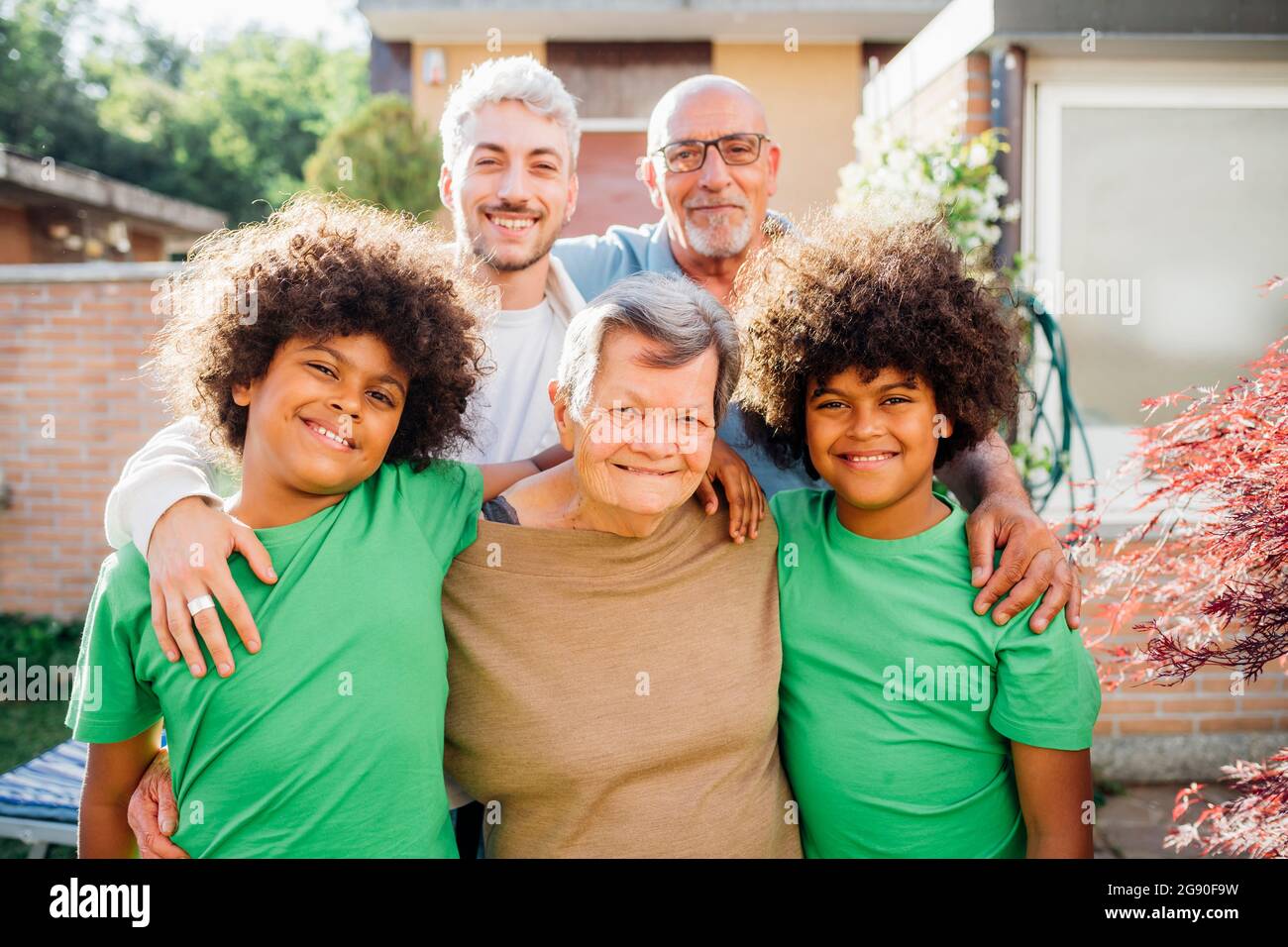 Smiling multi-ethnic family with arms around standing in back yard ...