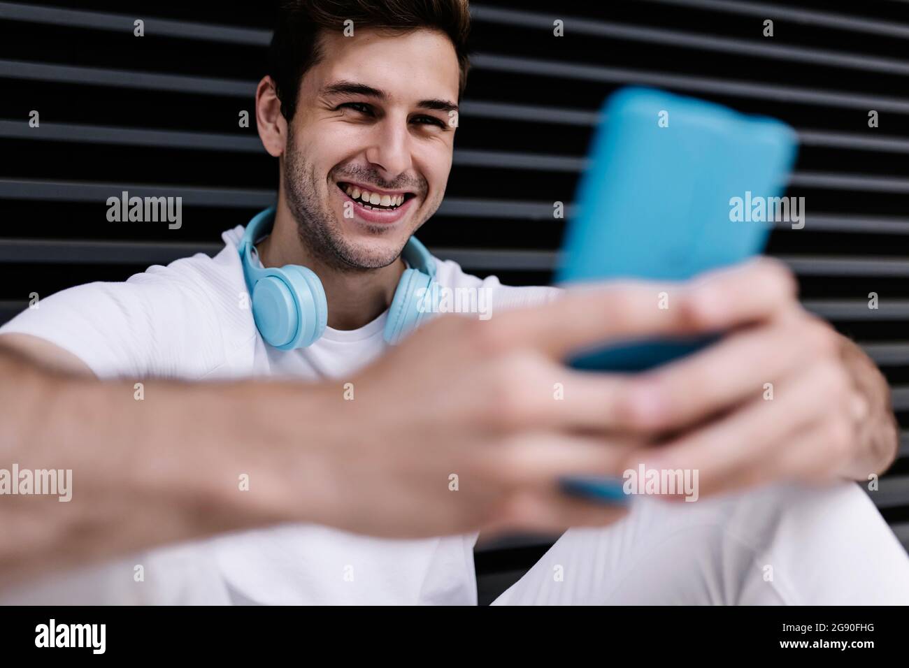 Happy man using smart phone while sitting in front of shutter Stock ...