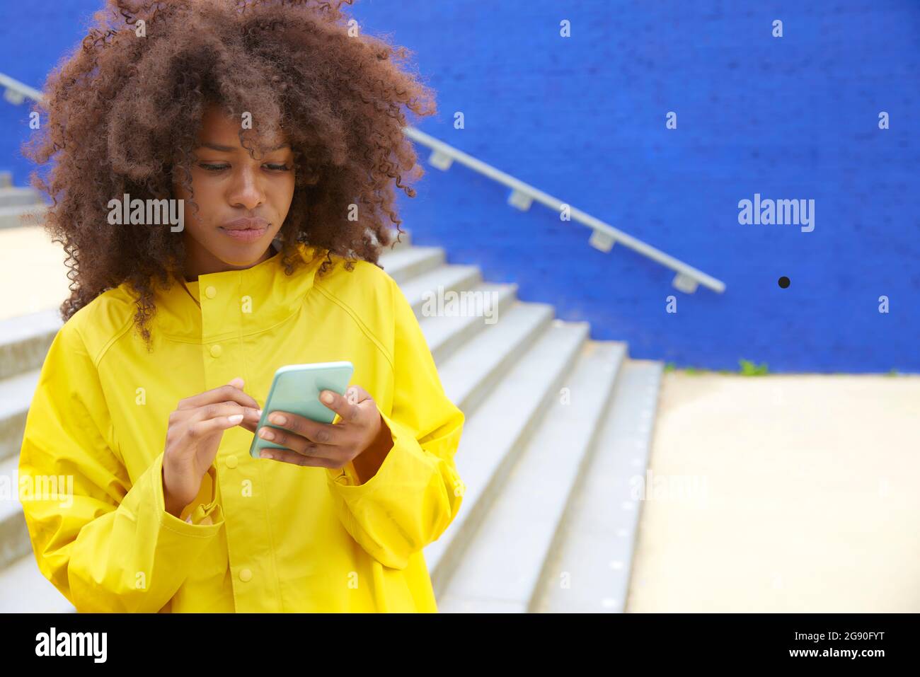 Young Afro woman text messaging through smart phone by steps Stock ...