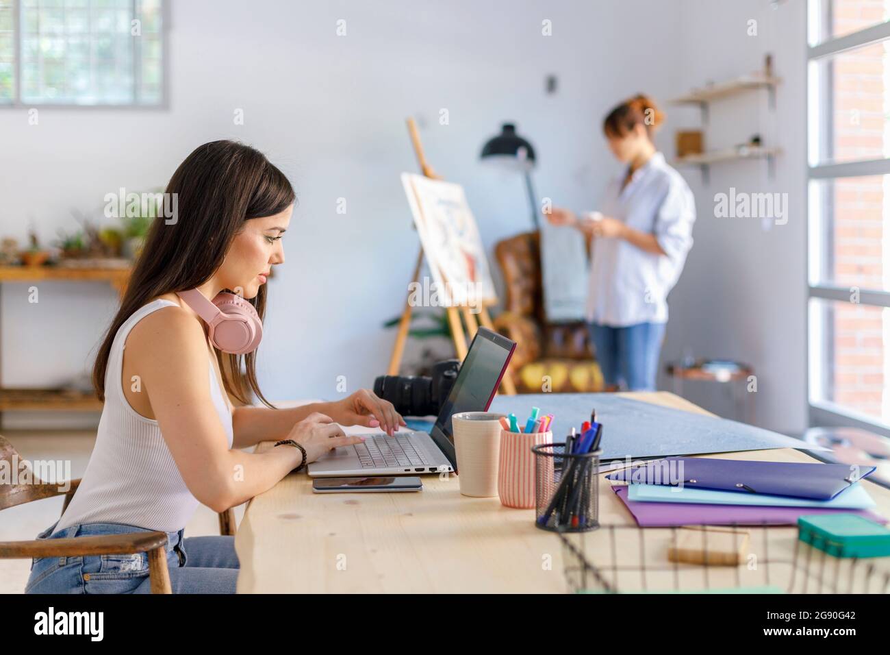 Female photographer using laptop while artist painting in studio Stock ...
