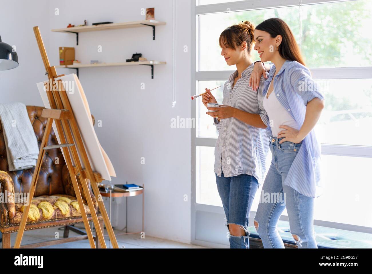 Female artists looking at painting while standing together in art ...
