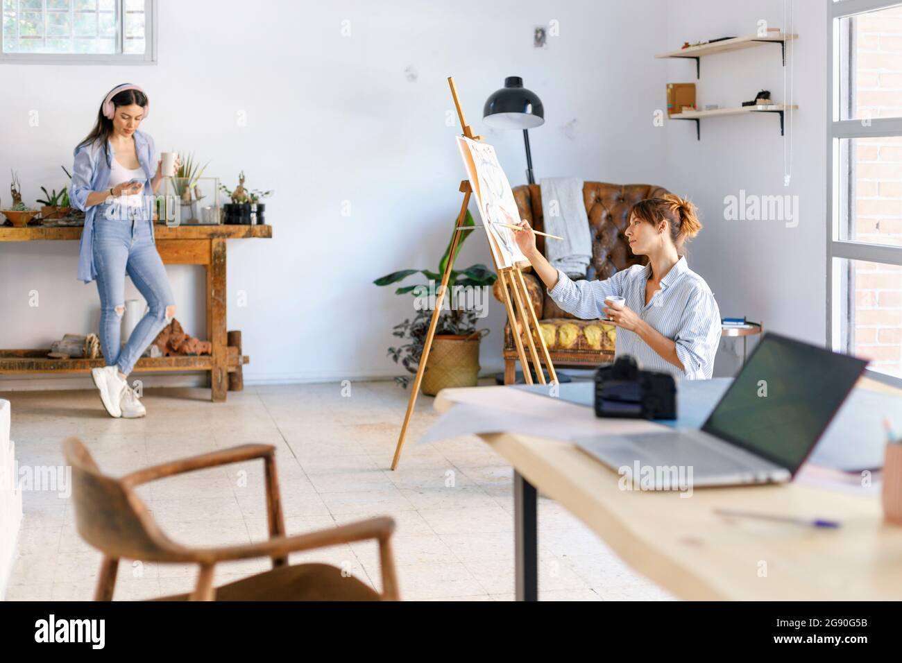 Female artist painting while photographer colleague listening music in ...