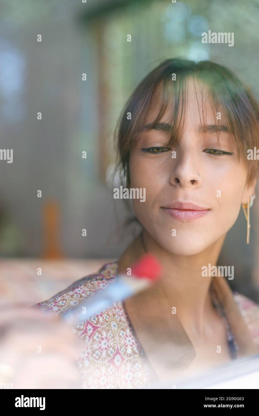 Young female artist holding paintbrush seen through studio window Stock ...
