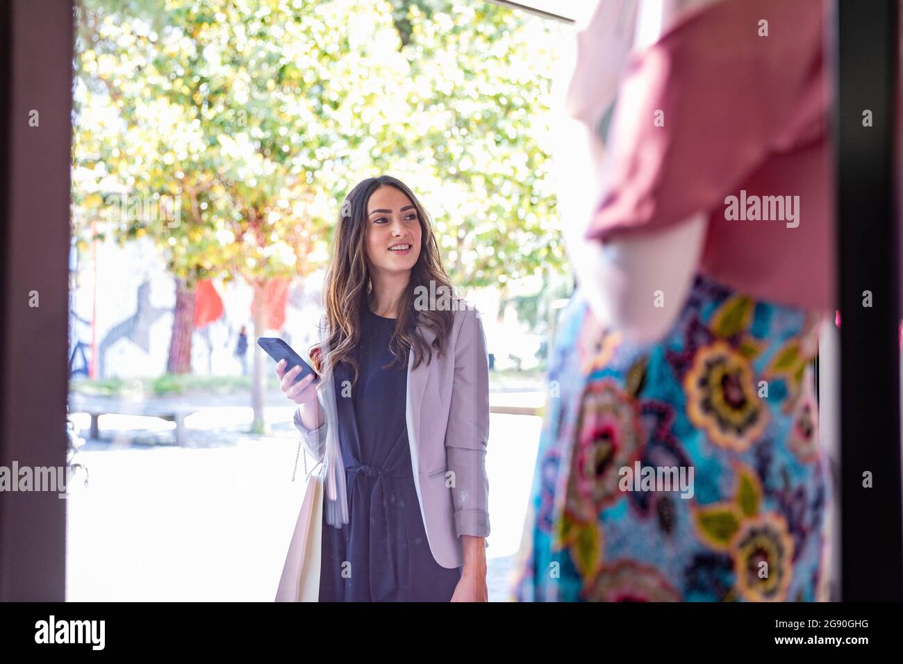 Woman holding smart phone while looking at mannequin outside boutique ...
