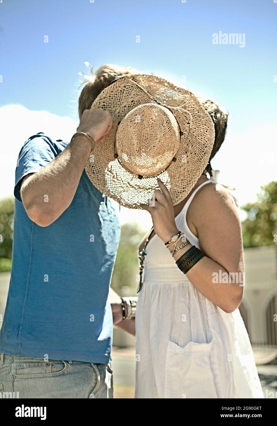 Couple covering face with straw hat while kissing during sunny day ...