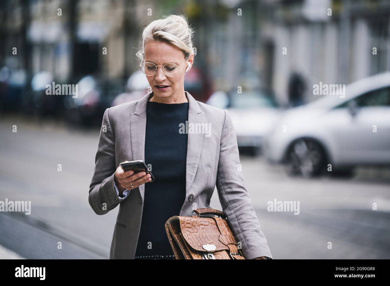 Blond female commuter holding bag while using smart phone Stock Photo ...