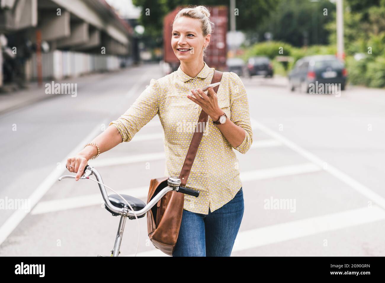 Female professional talking on mobile phone while wheeling bicycle ...