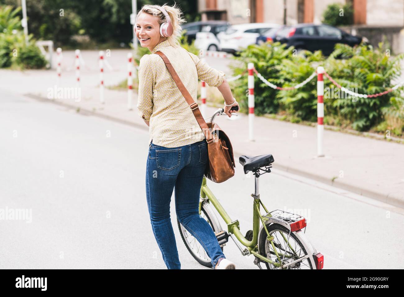 Happy female commuter wheeling bicycle while looking back over shoulder ...