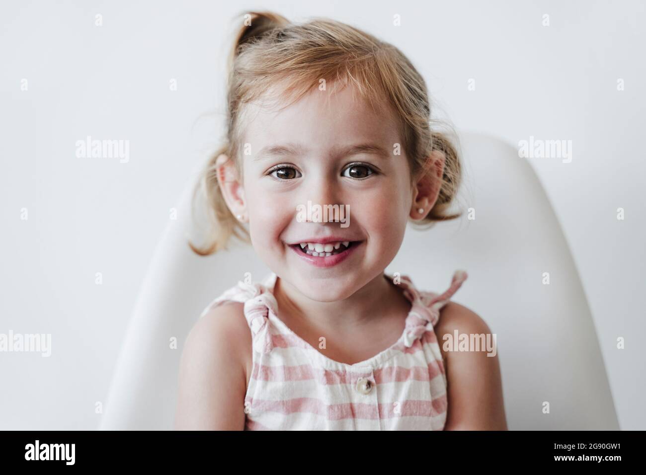 Cute girl smiling while sitting on chair in front of white background ...