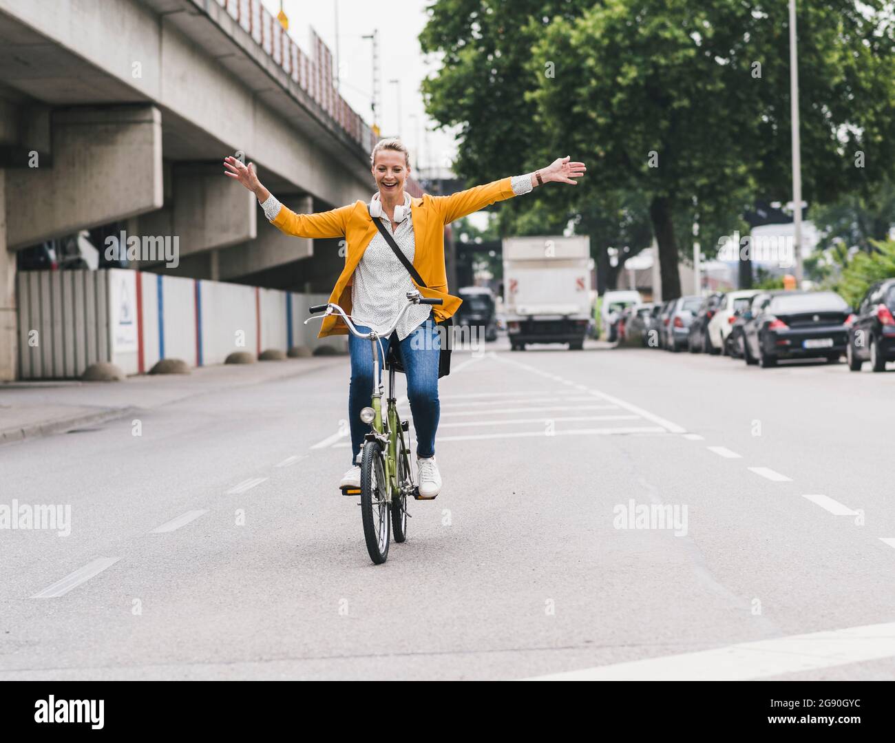 Carefree female commuter with arms outstretched riding bicycle on ...