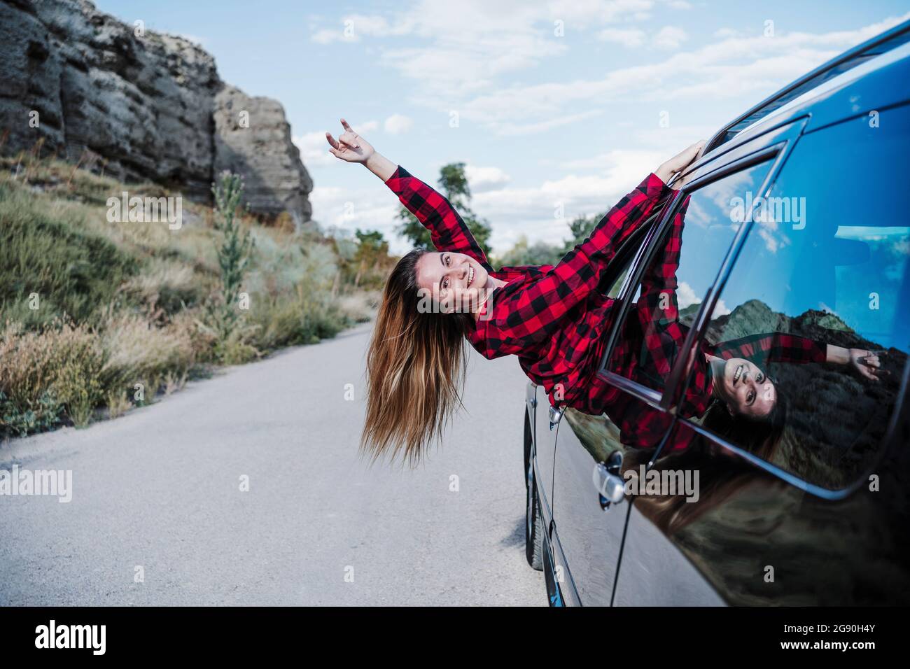 Smiling young woman with hand raised leaning from car window Stock ...
