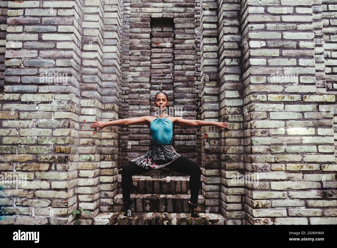 Female dancer doing balancing exercise amidst stone walls Stock Photo ...