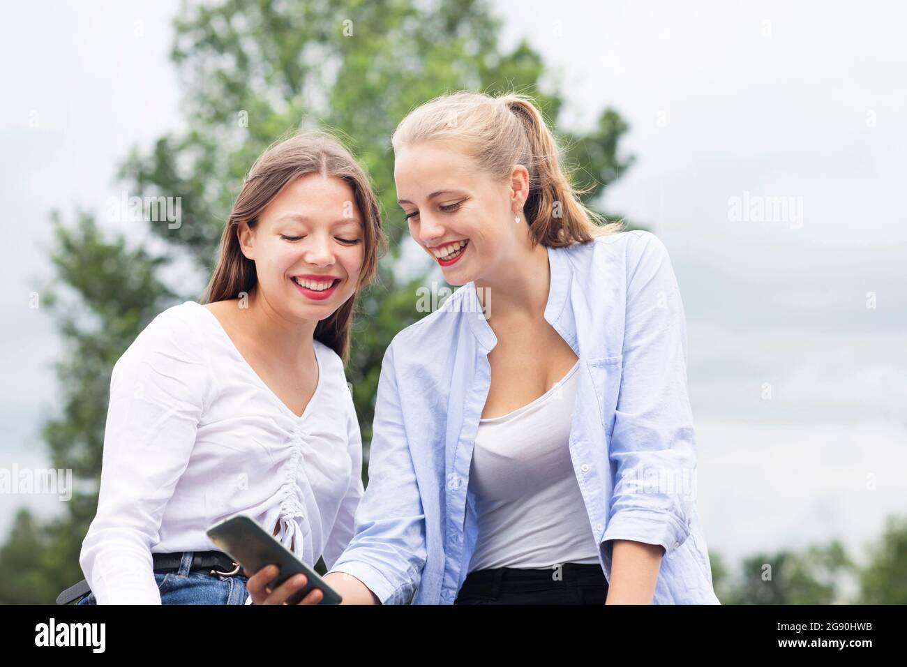 Happy blond woman sharing mobile phone with female friend Stock Photo ...