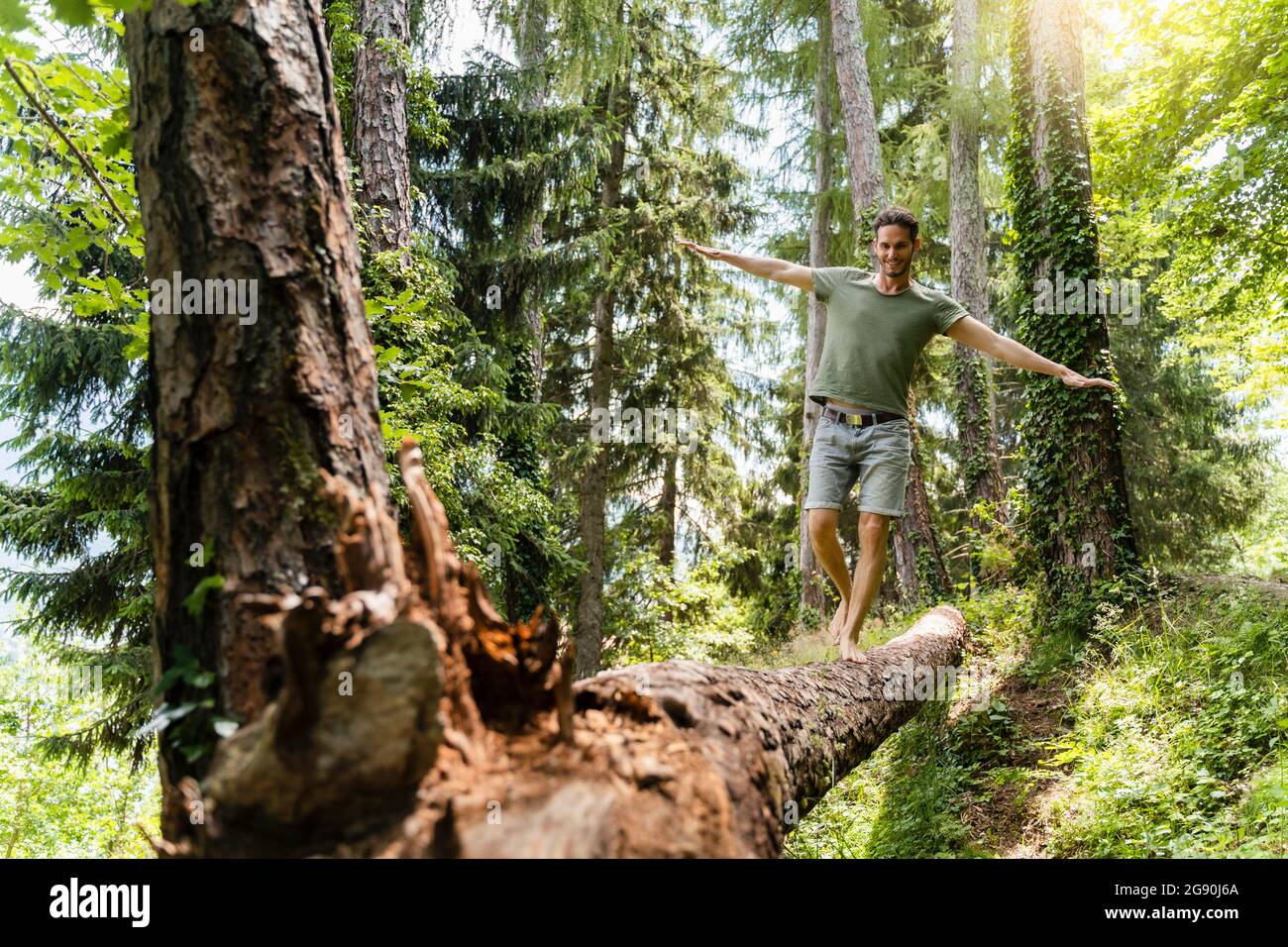 Playful man with arms outstretched walking on fallen tree Stock Photo ...