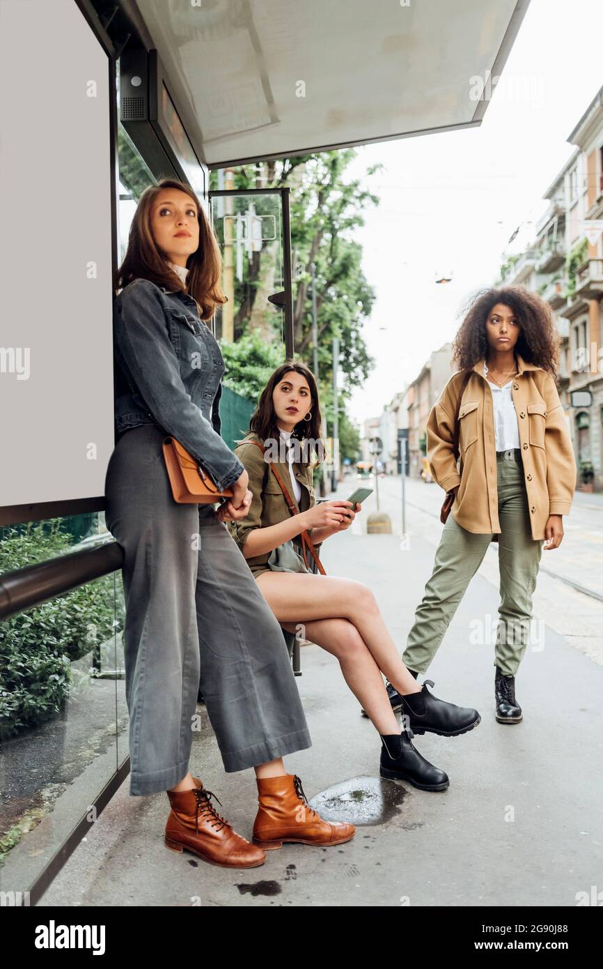 Young women waiting while standing at bus stop Stock Photo - Alamy