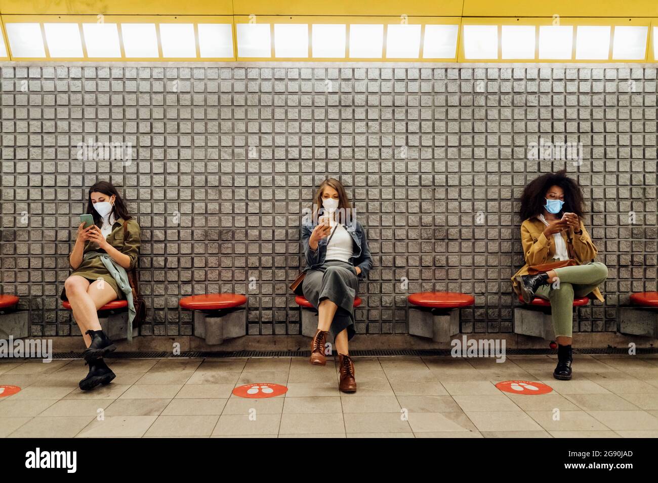 Friends with protective face mask using mobile phone while sitting at ...