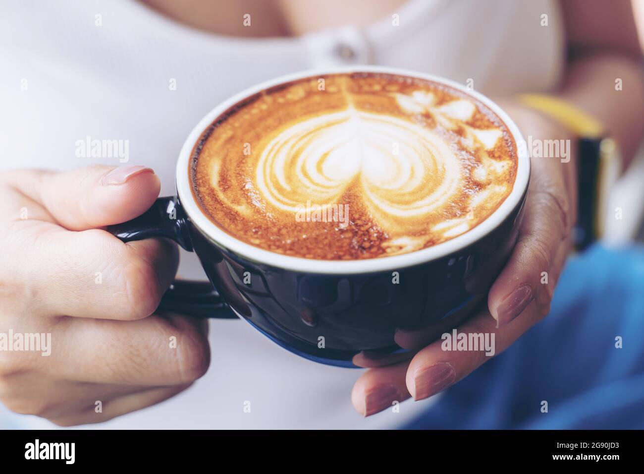 Close-up of a cup of coffee latte art on woman hand in coffee shop cafe ...