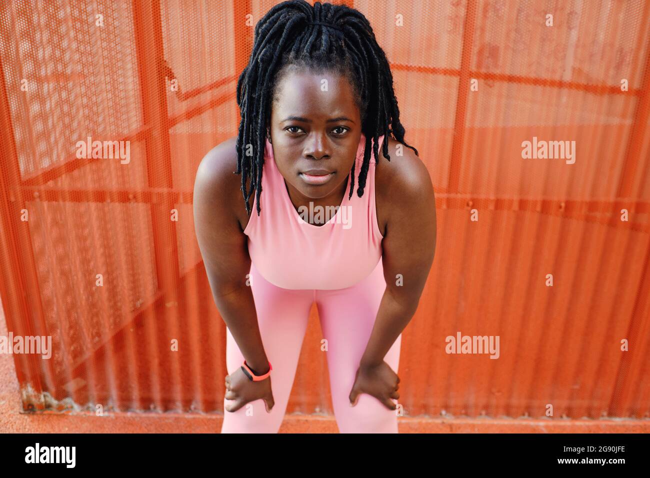 Confident young woman in sports clothing bending in front of corrugated ...