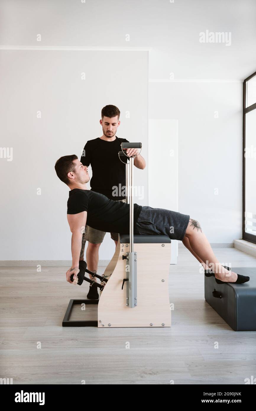 Male fitness instructor looking at man stretching at stability chair in ...