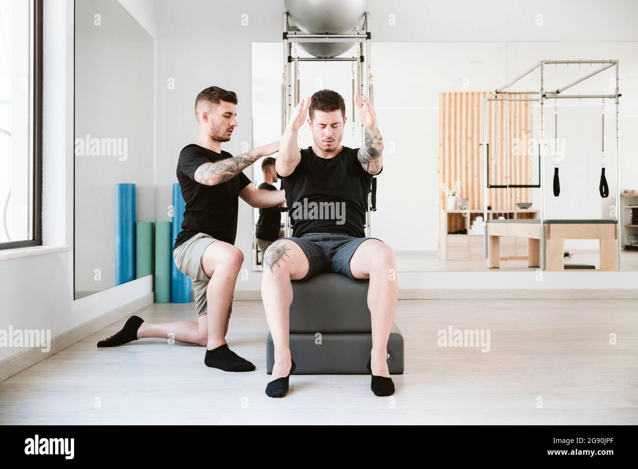 Male fitness instructor assisting man while practicing pilates in ...
