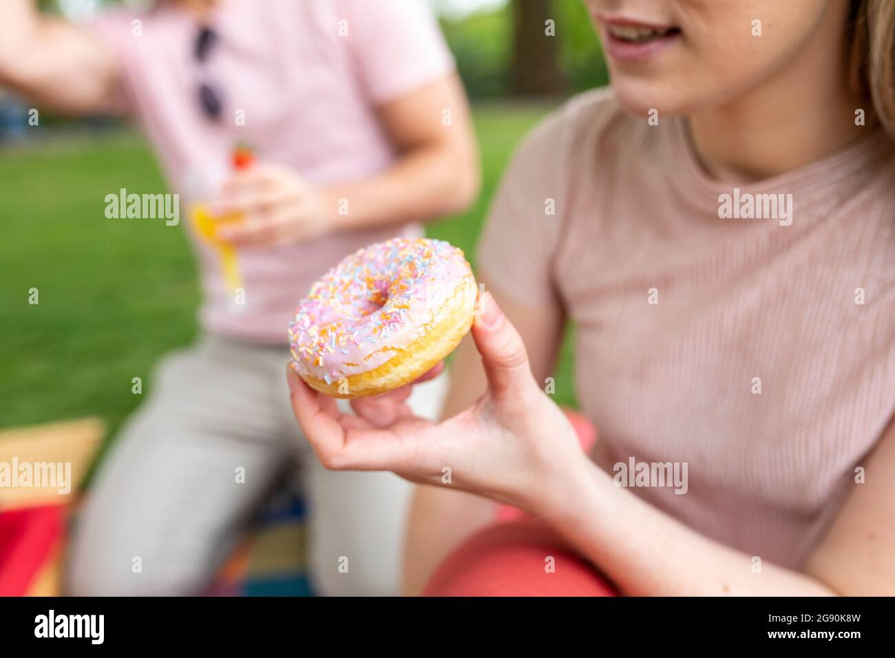Woman holding doughnut with friend sitting in background at park Stock ...