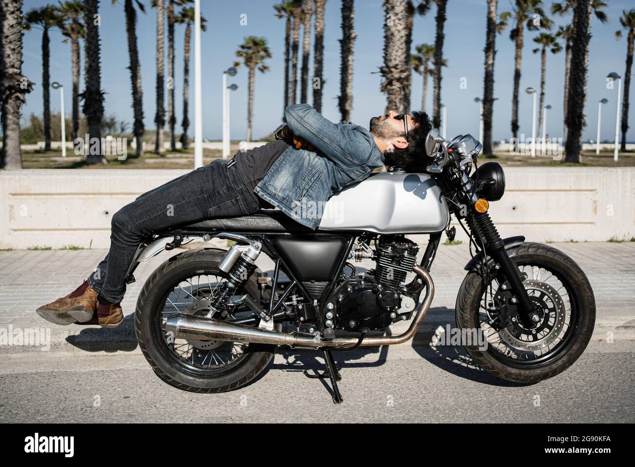Young man lying on motorcycle with arms crossed during sunny day Stock ...