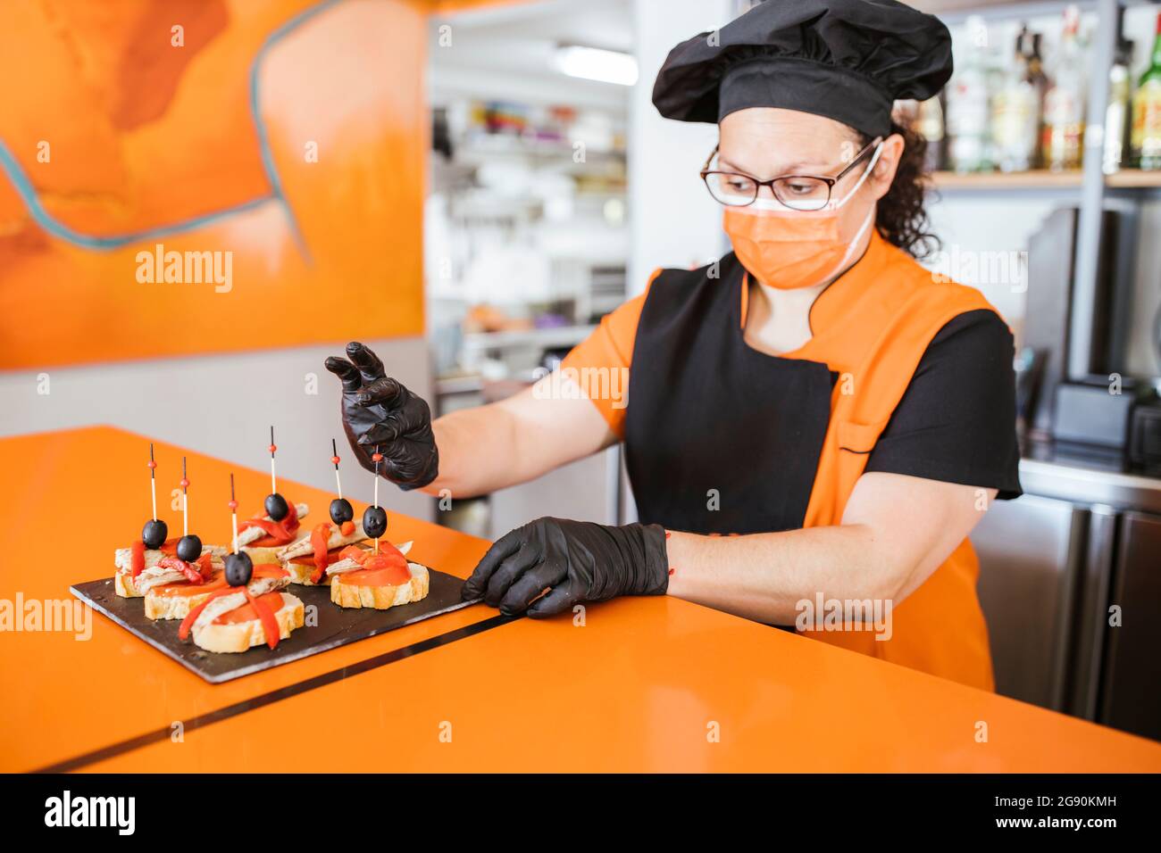 Female chef putting toothpicks in sandwich at cafeteria during COVID-19 ...