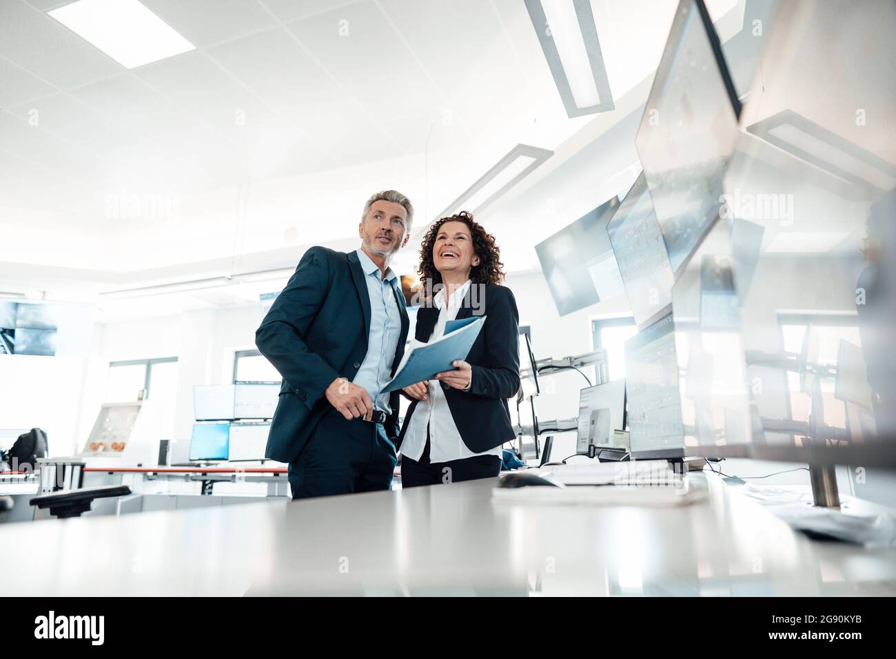 Male and female experts smiling while standing together in control room ...