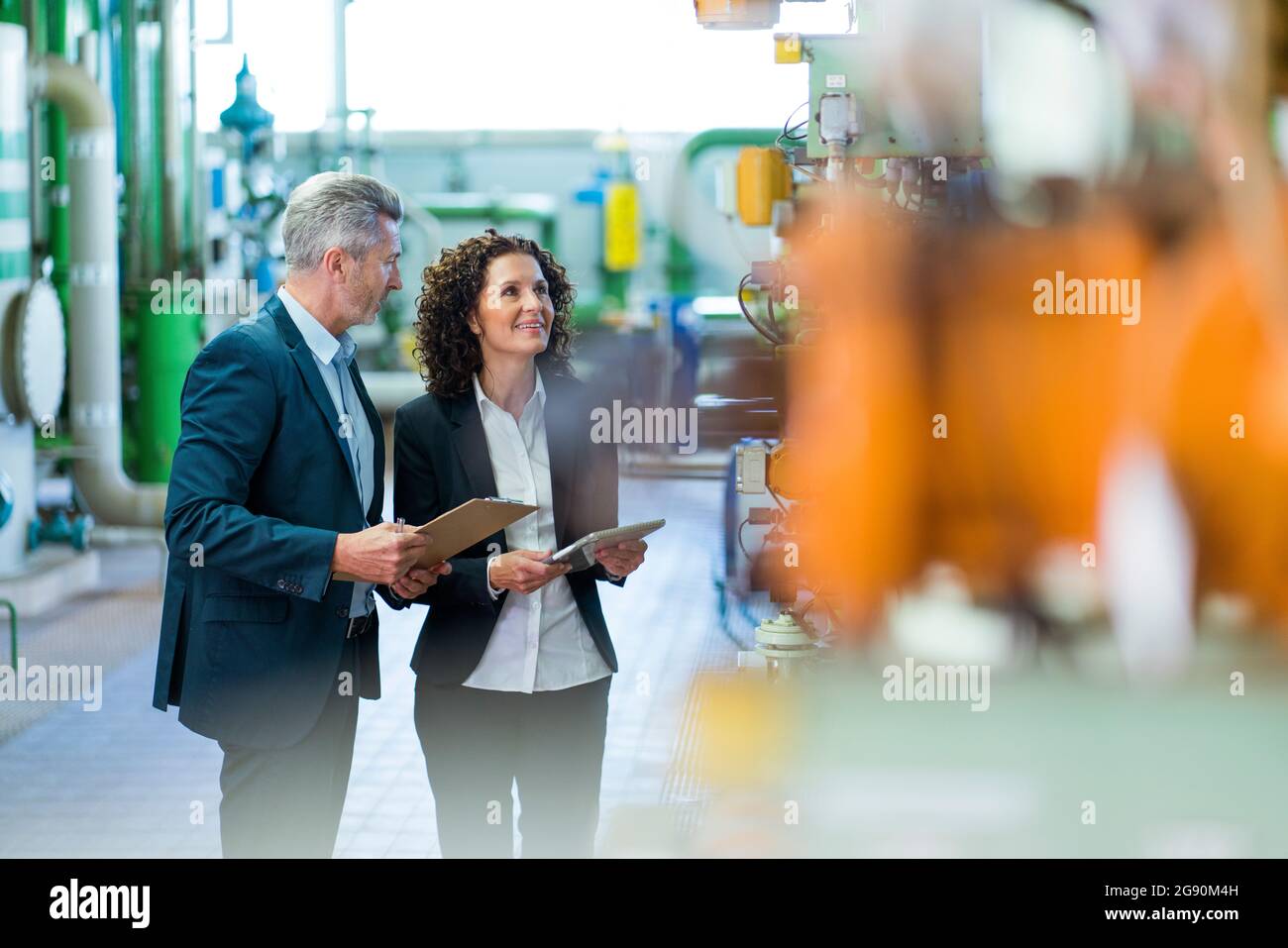 Male and female inspectors checking machine while standing in industry ...