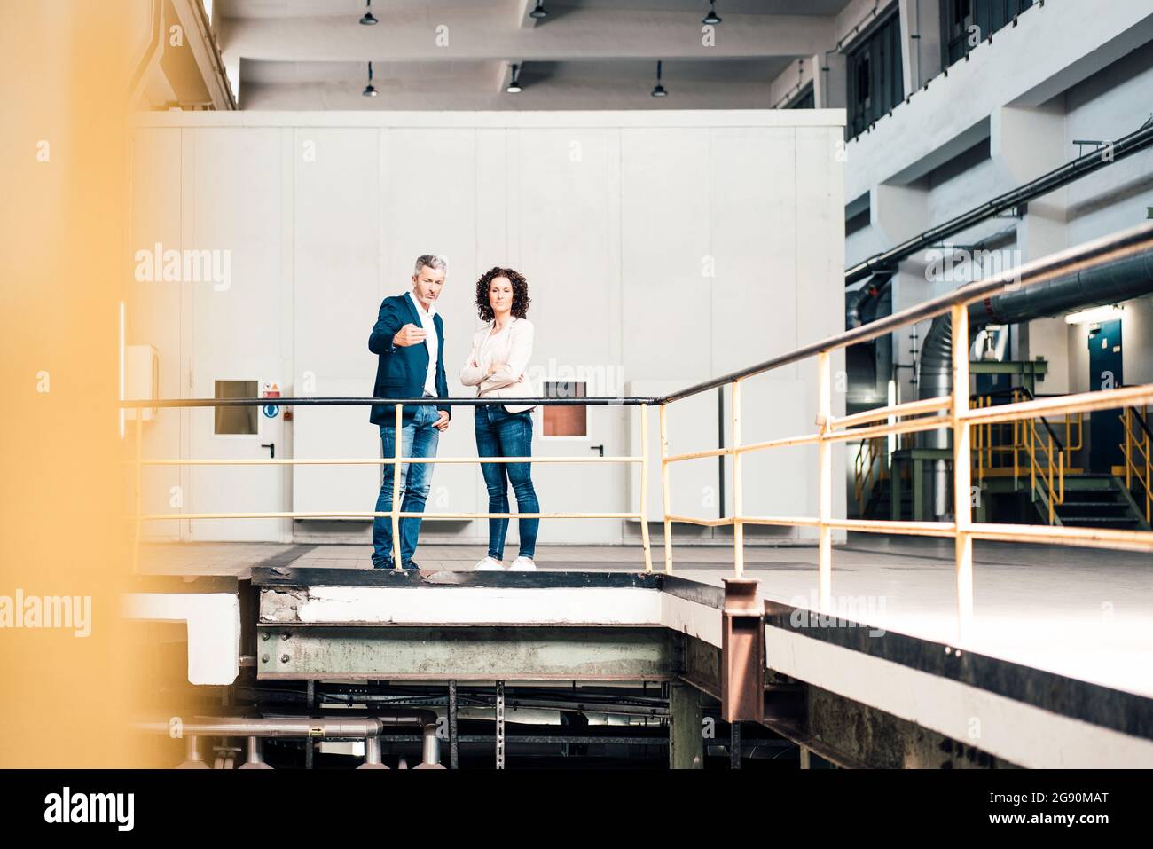 Businessman explaining colleague while standing by railing in industry ...
