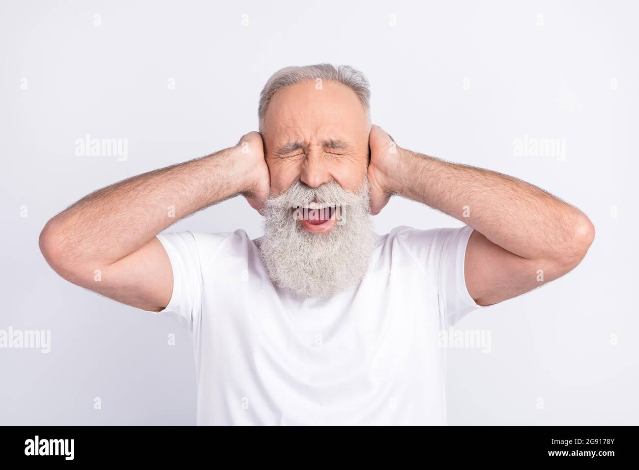 Portrait of attractive crazy middle-aged man closing ears shouting ...