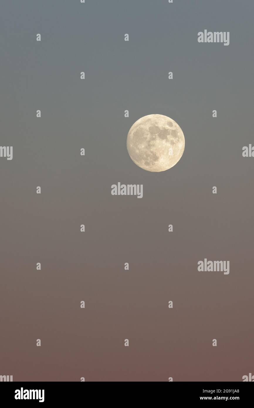 A brightly glowing full moon in a clear sky of pastel blue fading into ...