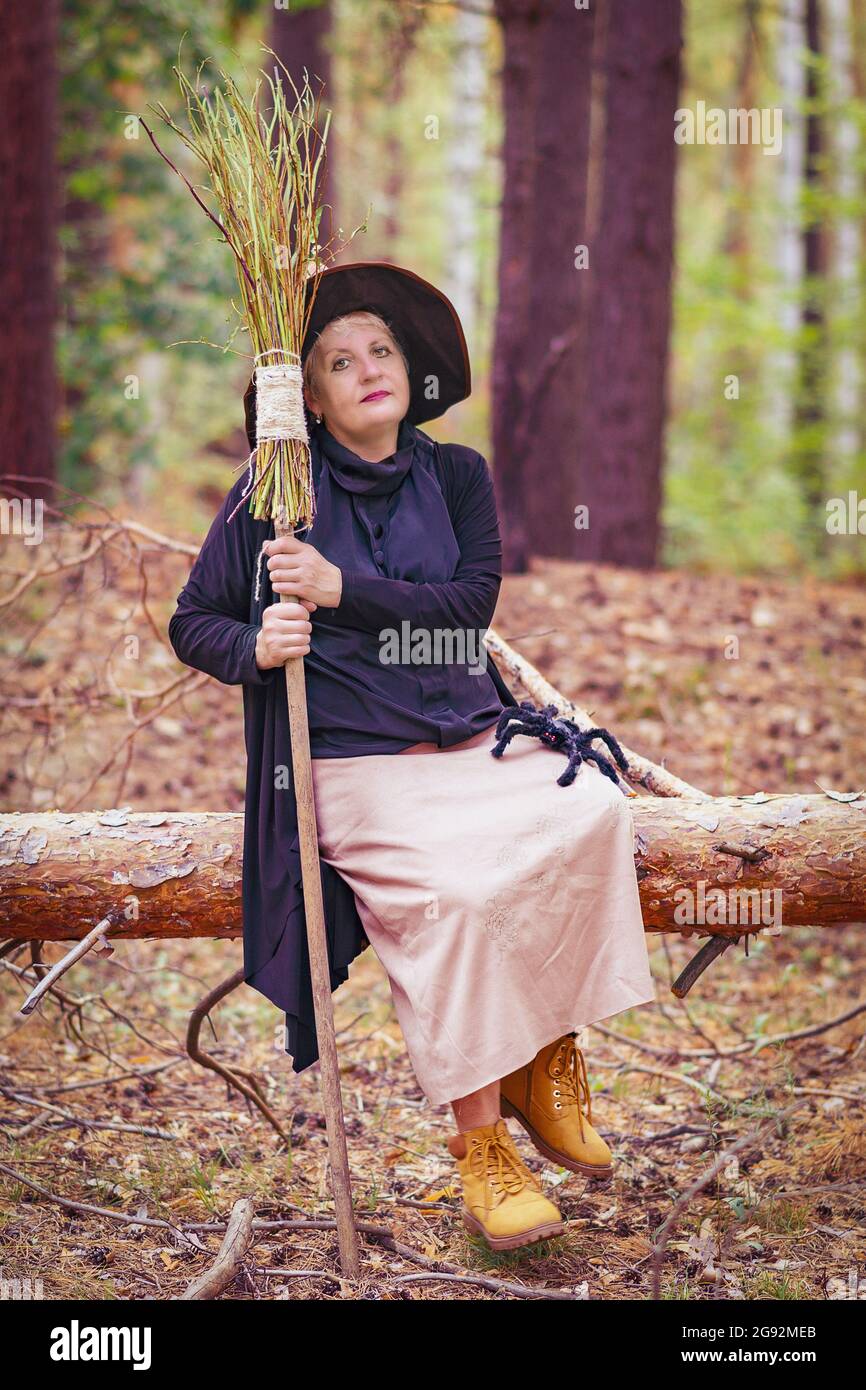An elderly witch in a hat in the woods, sitting on a tree trunk, legs ...