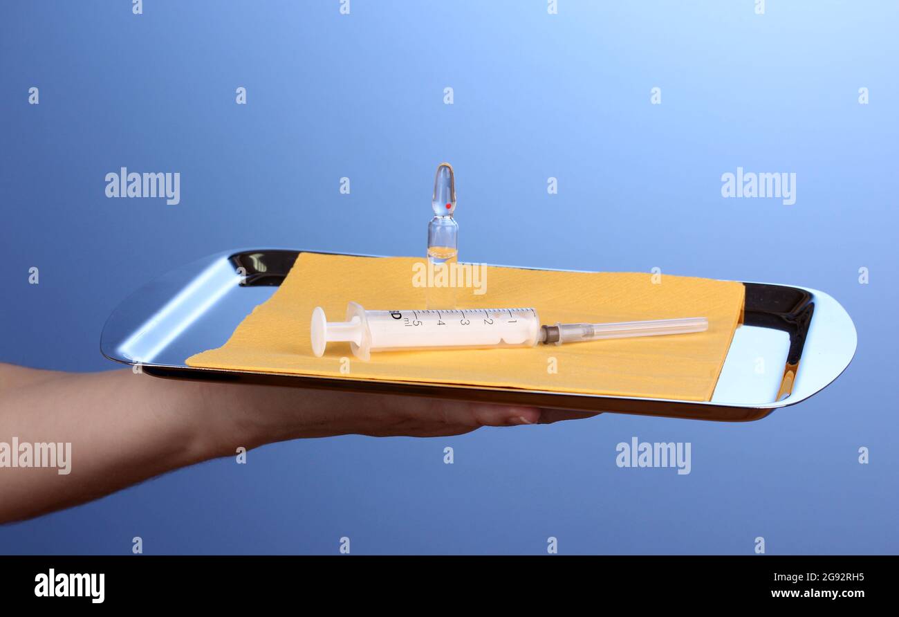 Hand holding tray with syringe and medicines on blue background Stock ...