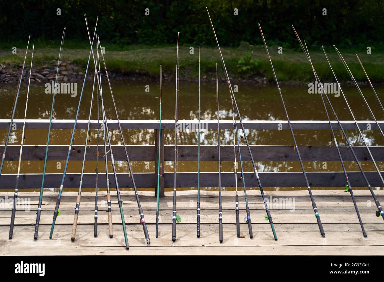 Many fishing rods on the wooden pier by the river or lake on a sunny ...