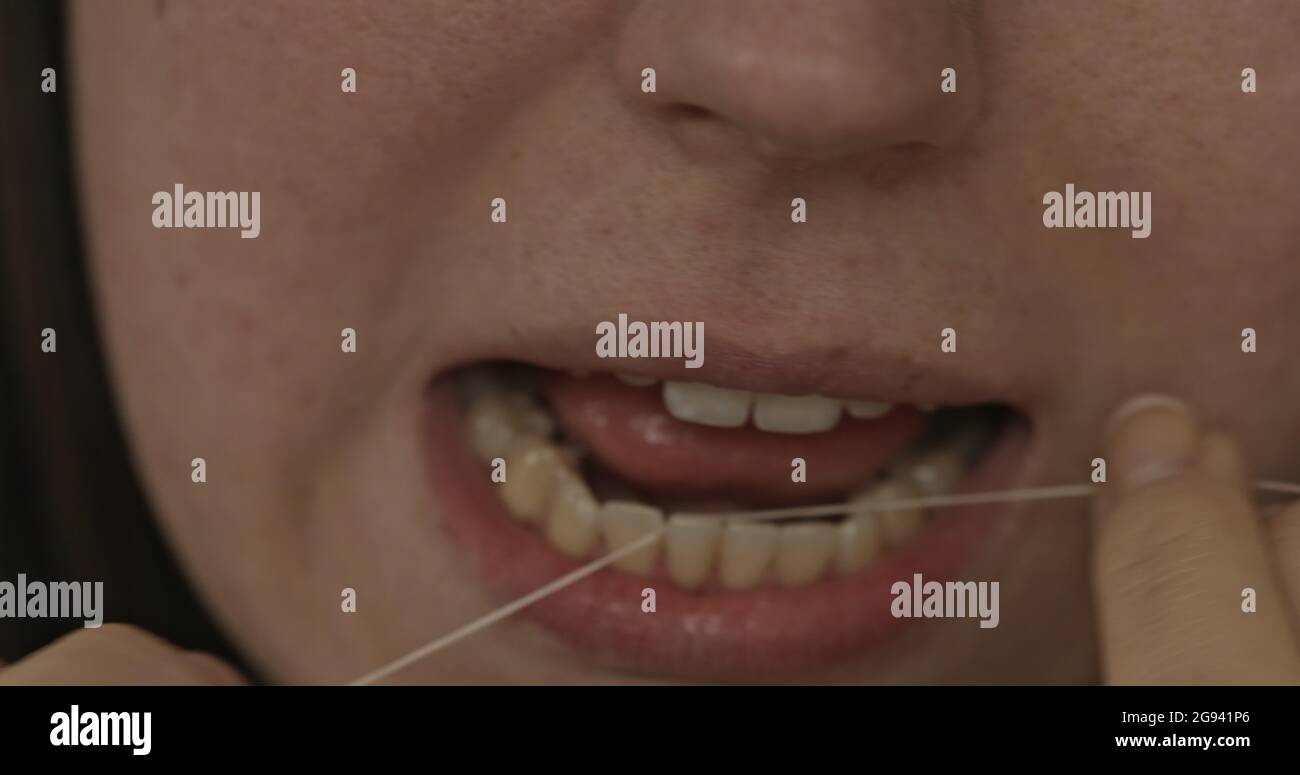 Woman flossing teeth with dental floss at her bathroom. Macro shoot ...