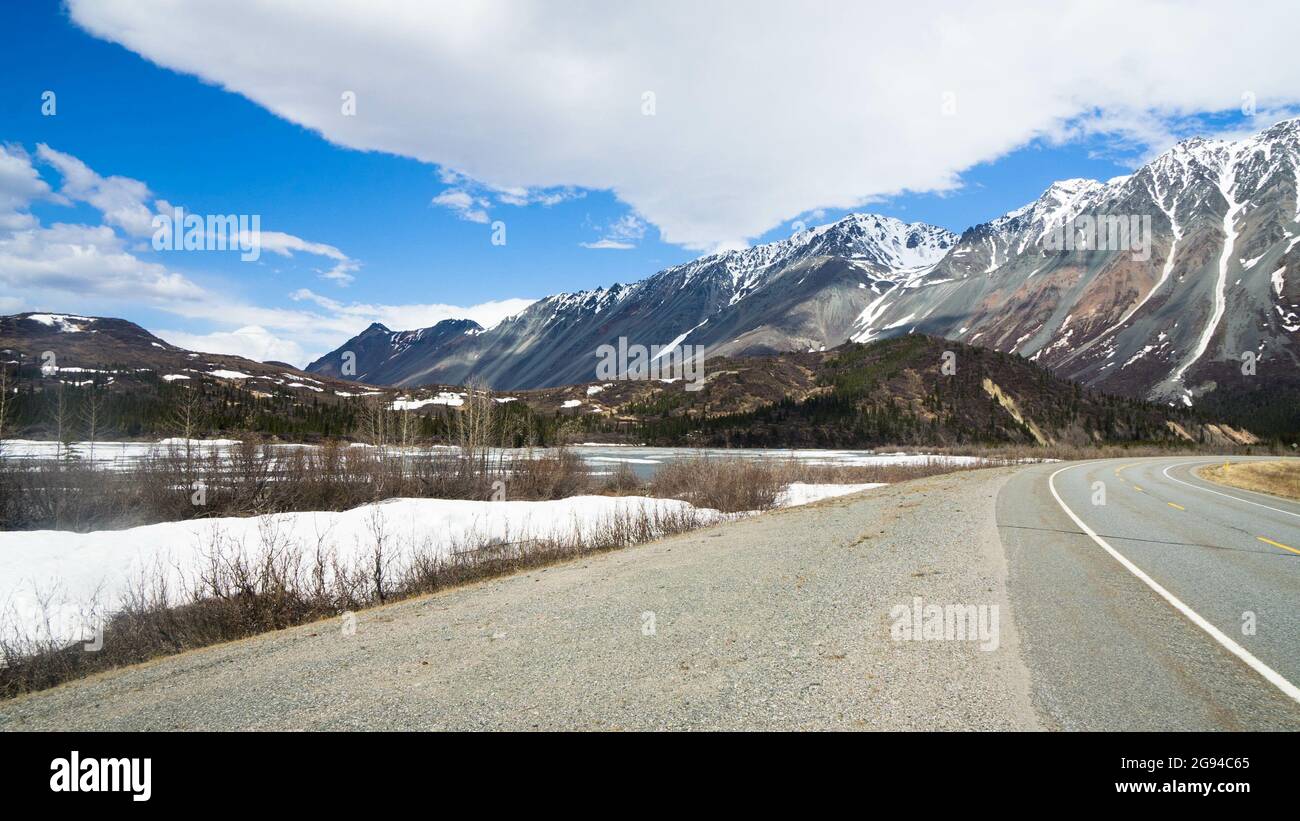 Road and roadside greenery covered in snow under clouds - mountains in ...