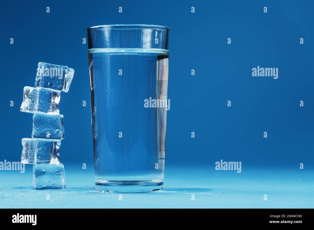 Ice cubes tower with a glass of cold and clean water on a blue ...