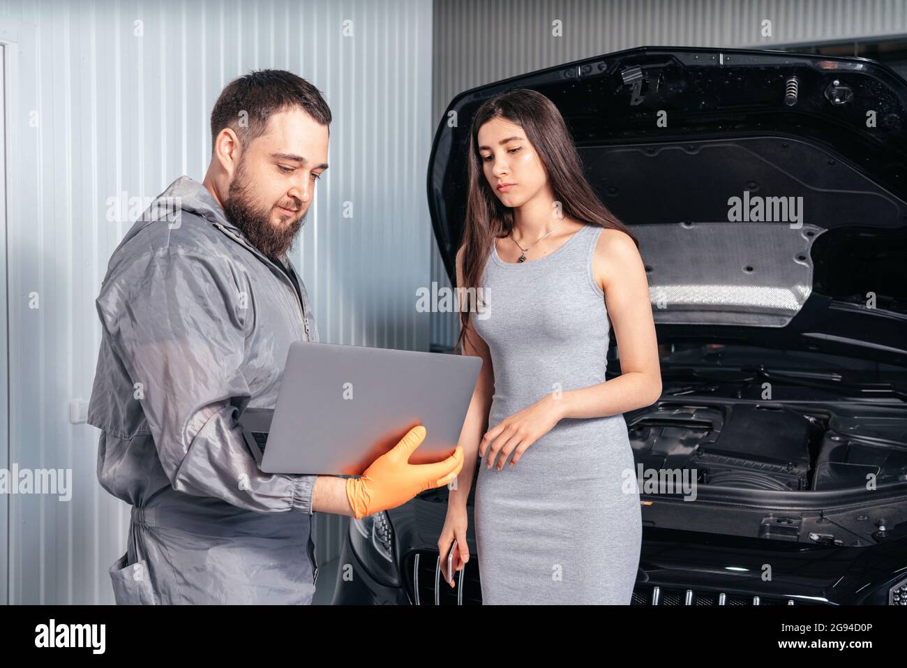 Car mechanic communicating with a female customer while using laptop ...