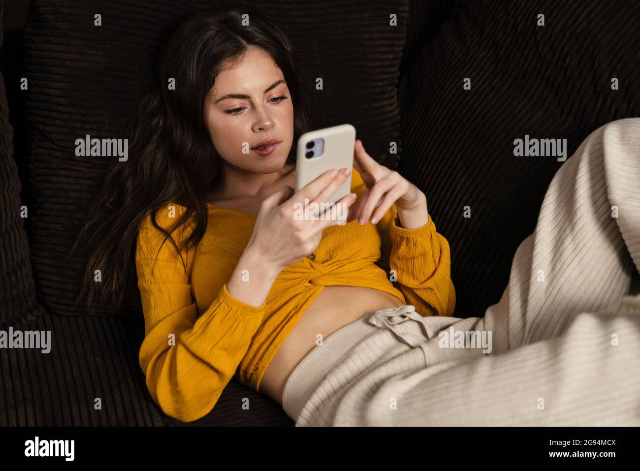 Young brunette woman using mobile phone while laying on a couch Stock ...